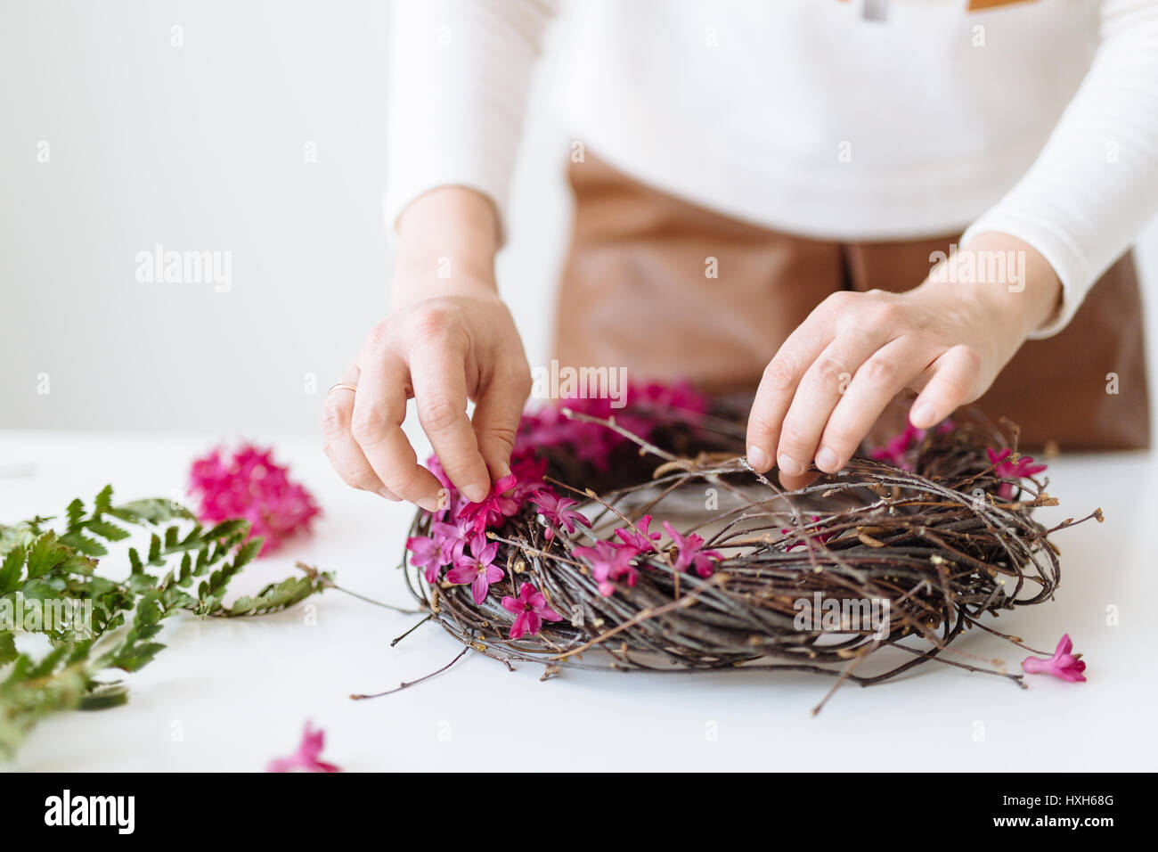 Girl florist makes a bouquet in the form of a nest on a white table ...