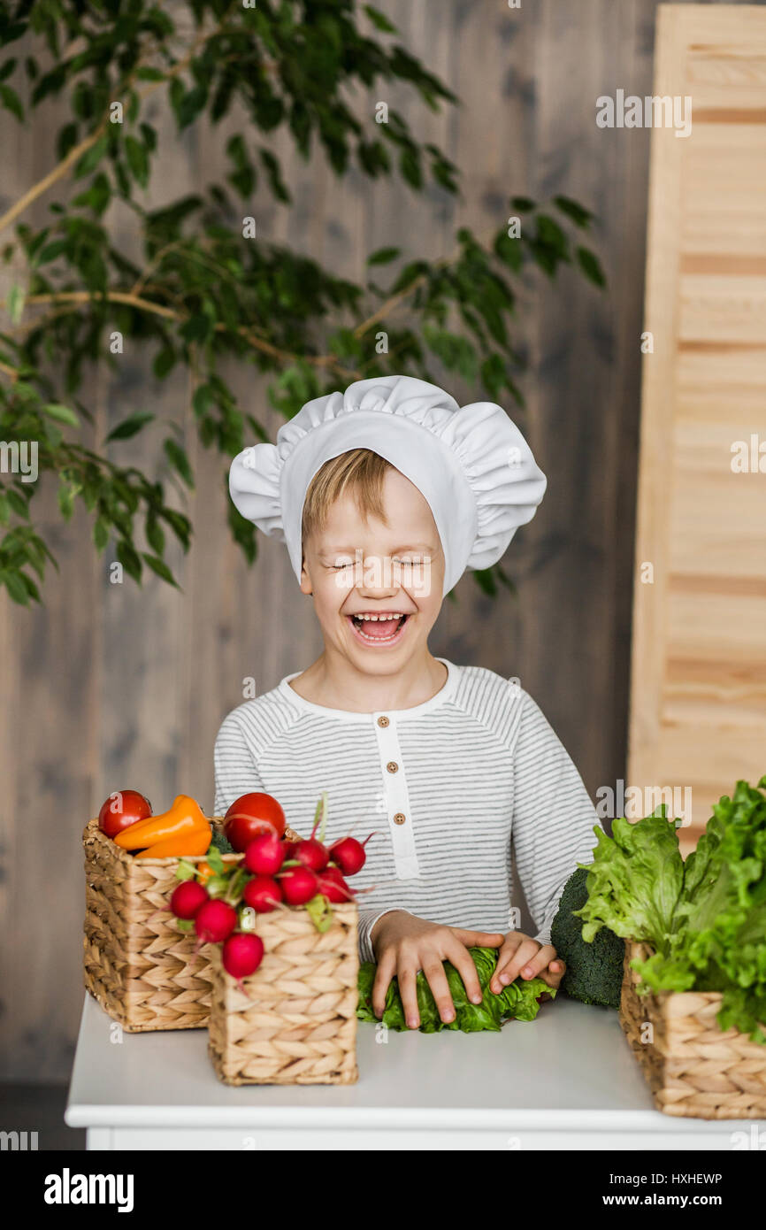 Handsome little kid in chef uniform with vegetables. Cooking in kitchen ...