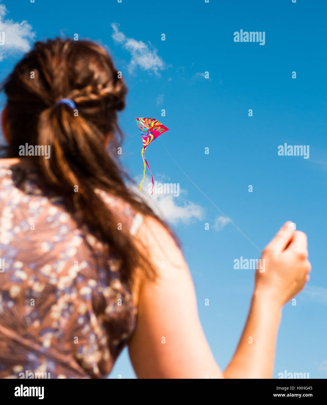 a kite flys in a bright blue sky with white fluffy clouds. The strings ...