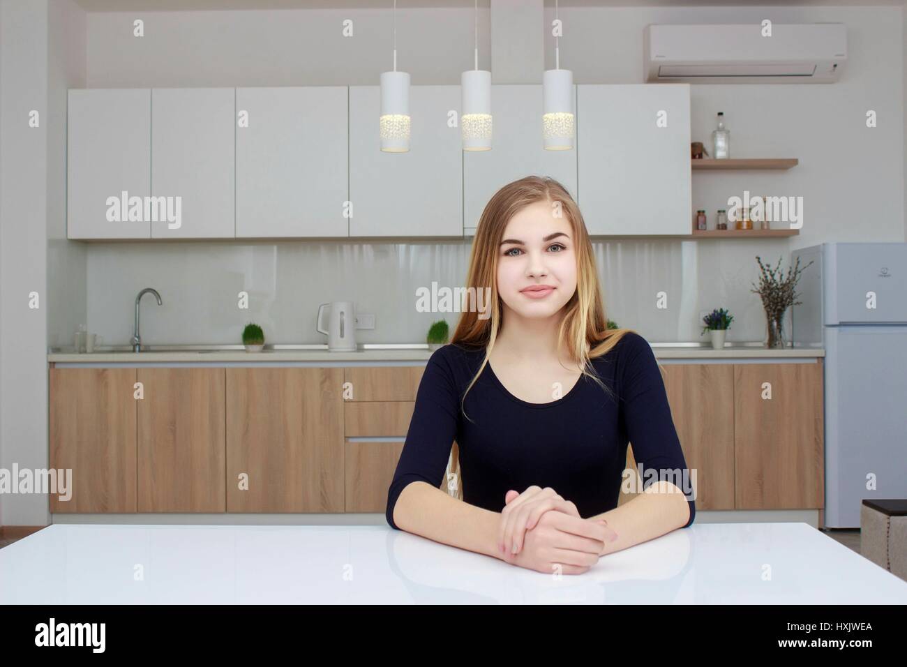 Young woman sitting a table in the kitchen Stock Photo - Alamy