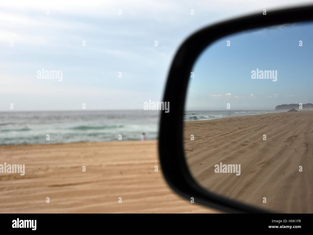 Reflections in a side view mirror of a car driving on the beach. Rear ...