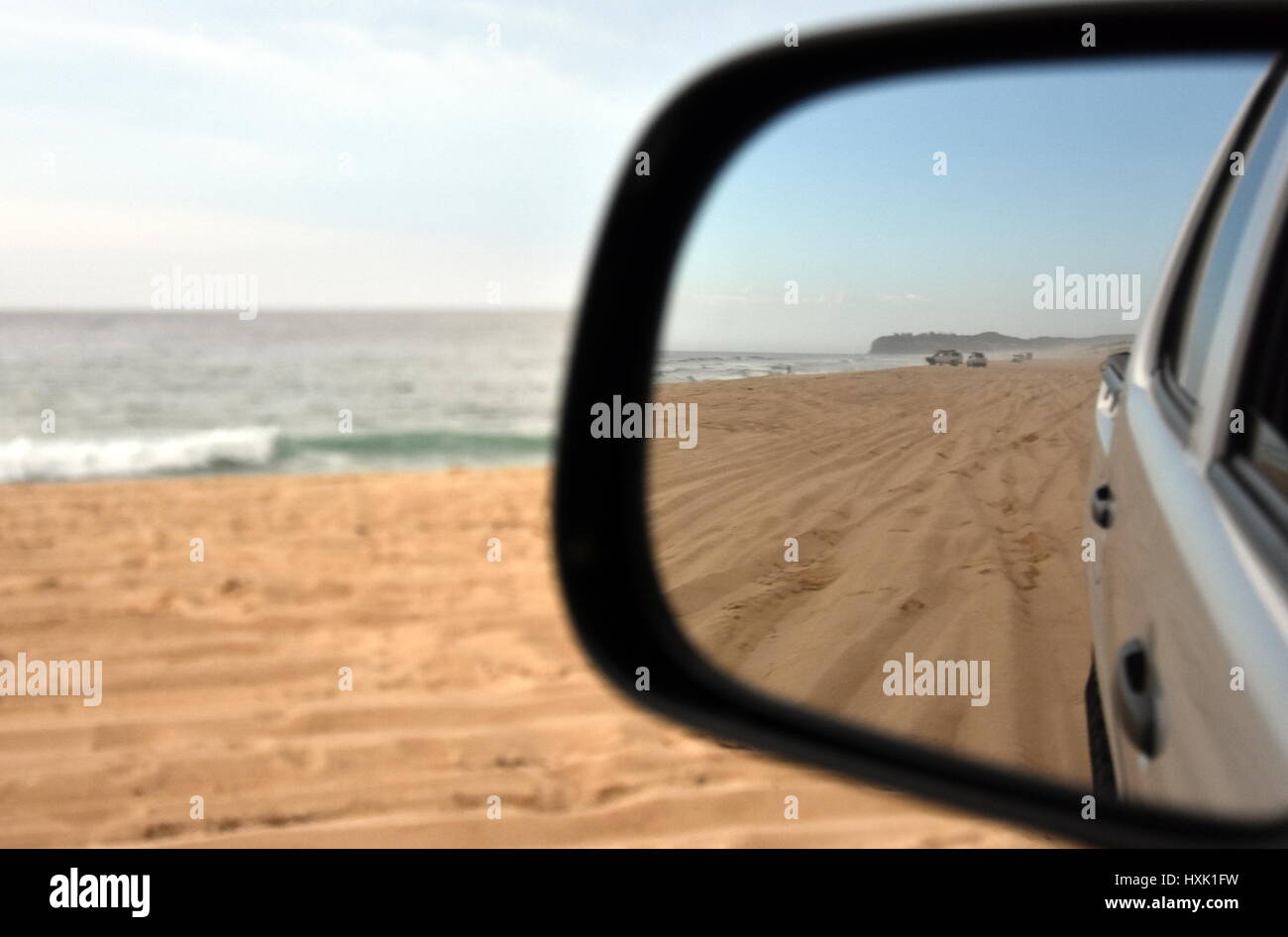 Reflections in a side view mirror of a car driving on the beach. Rear ...