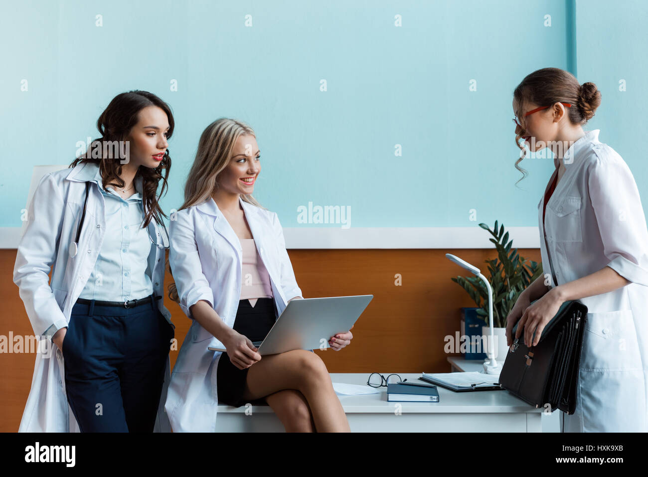 doctor closing briefcase while colleagues using laptop at workplace ...