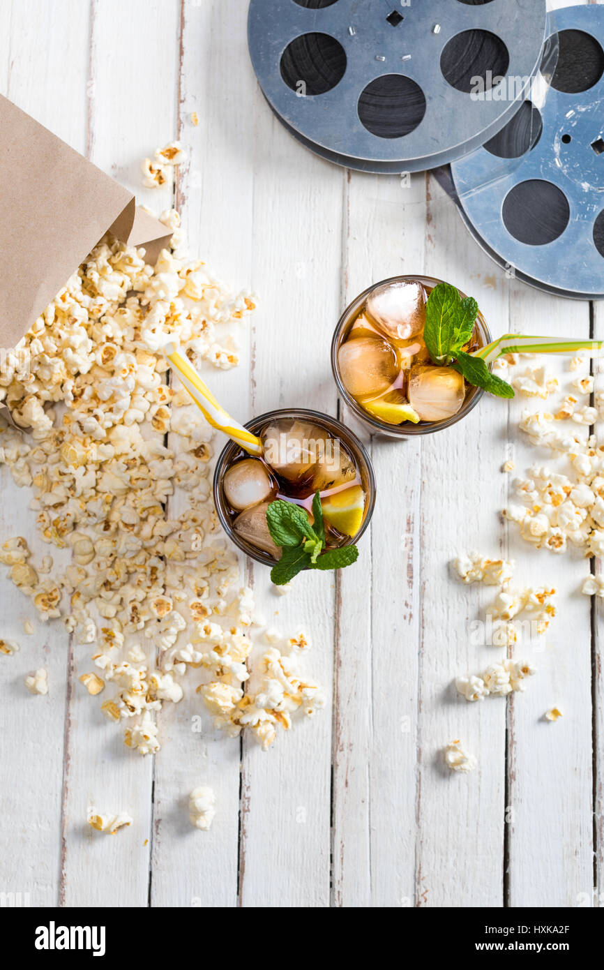 Top view of popcorn with iced tea in glasses and film reels on table ...