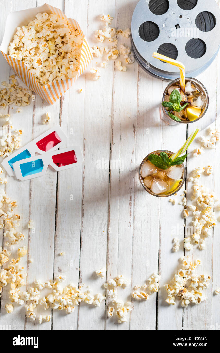 Top view of popcorn with iced tea, film reels and 3D glasses on table ...