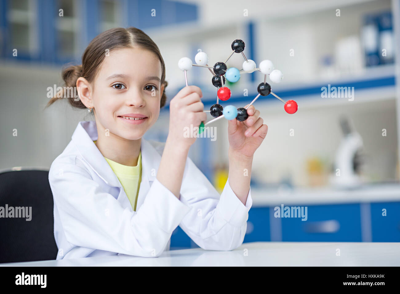 Girl scientist in lab coat holding molecular model and smiling at ...