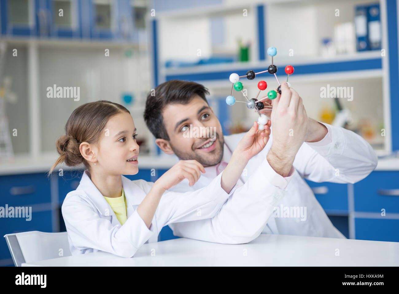 Smiling teacher and student scientists looking at molecule model in lab ...