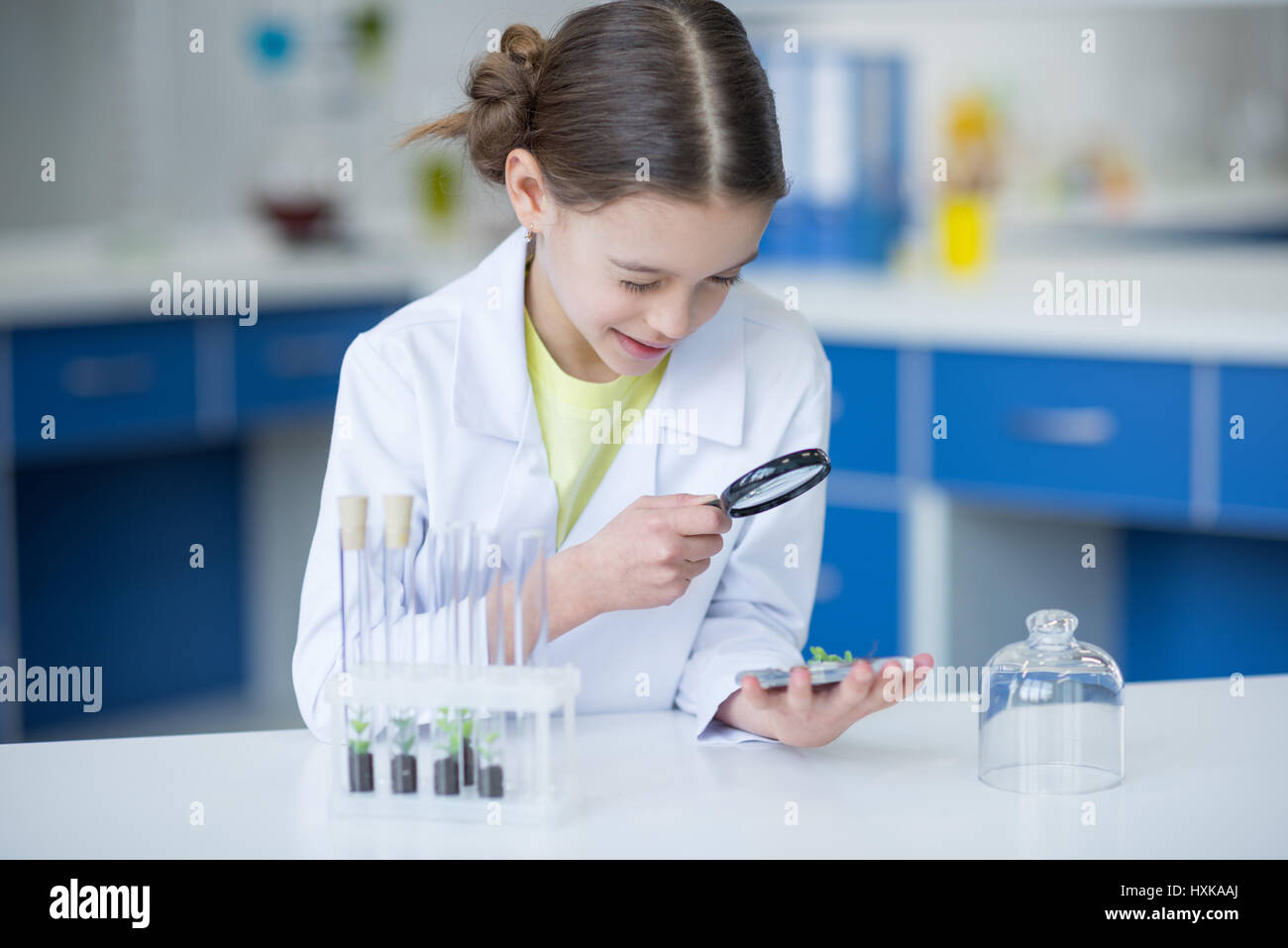 Smiling girl scientist holding magnifier and looking at green plant in ...