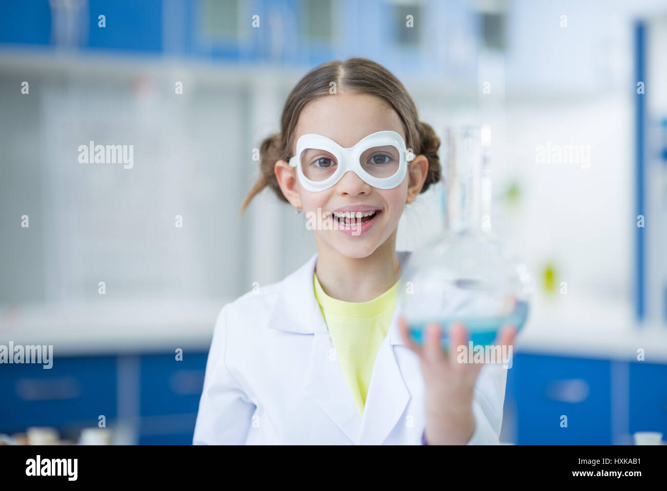 Little girl scientist in protective glasses holding flask and smiling ...