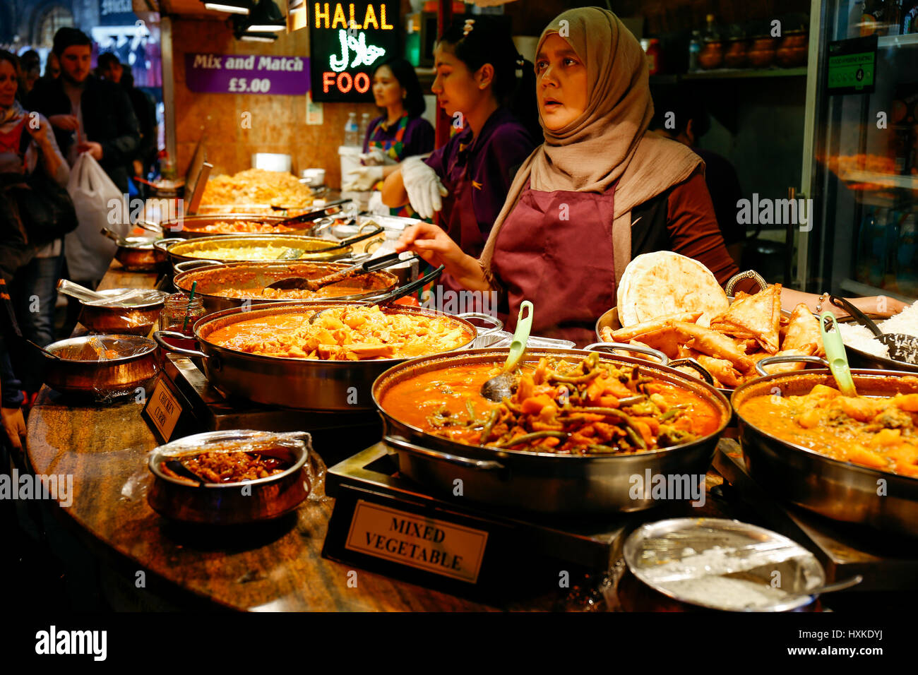 Traders at a market stall selling curry and varieties of cooked foods ...