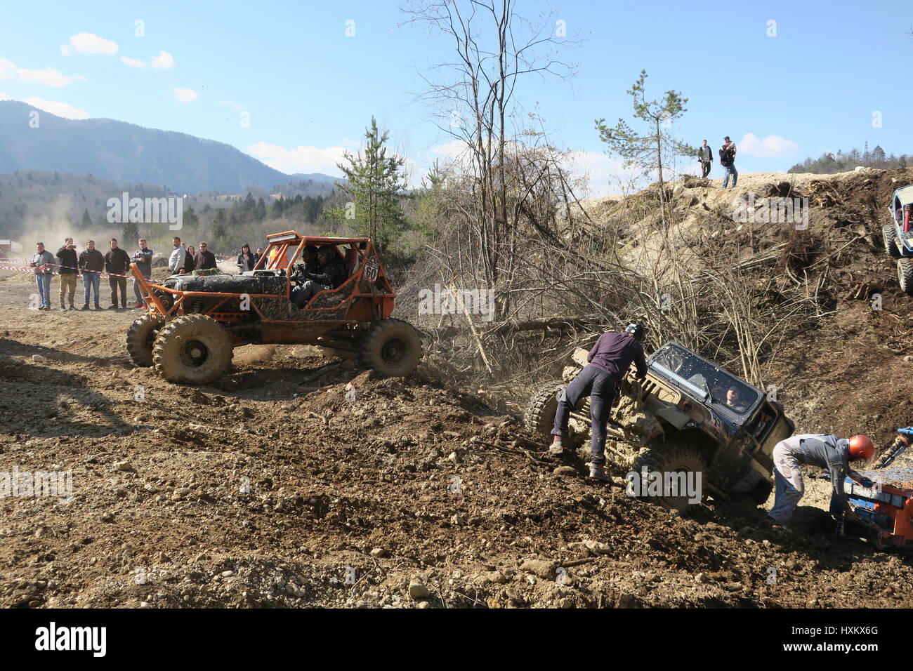 Three off-road cars are pushed uphill, co-driver pulling rope at ...