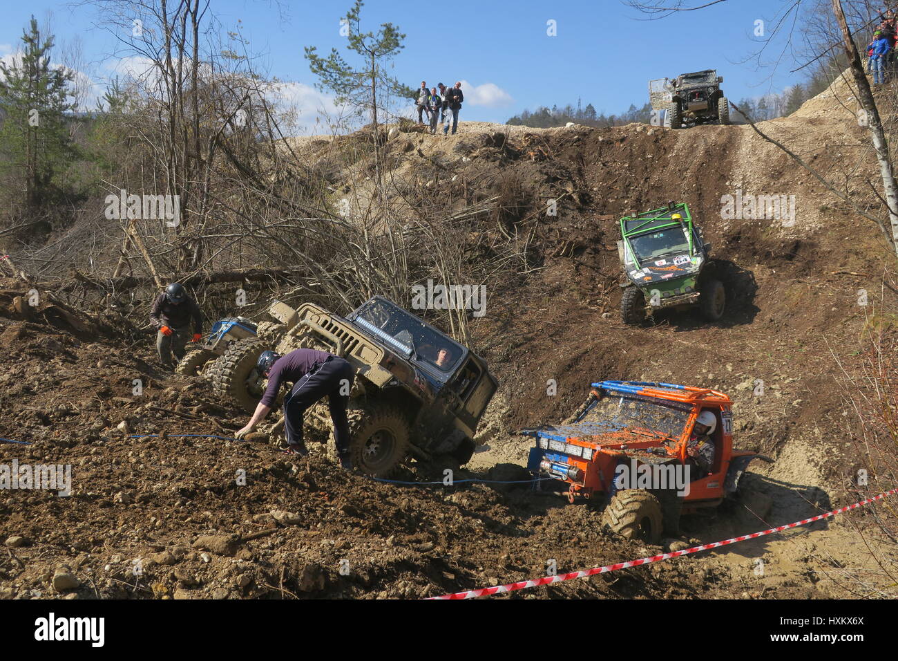 Three off-road cars are pushed uphill, co-driver pulling rope at ...