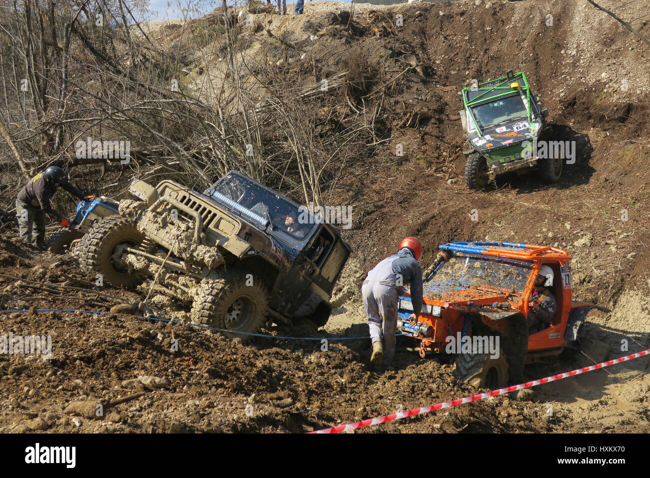 Three off-road cars are pushed uphill, co-driver pulling rope at ...