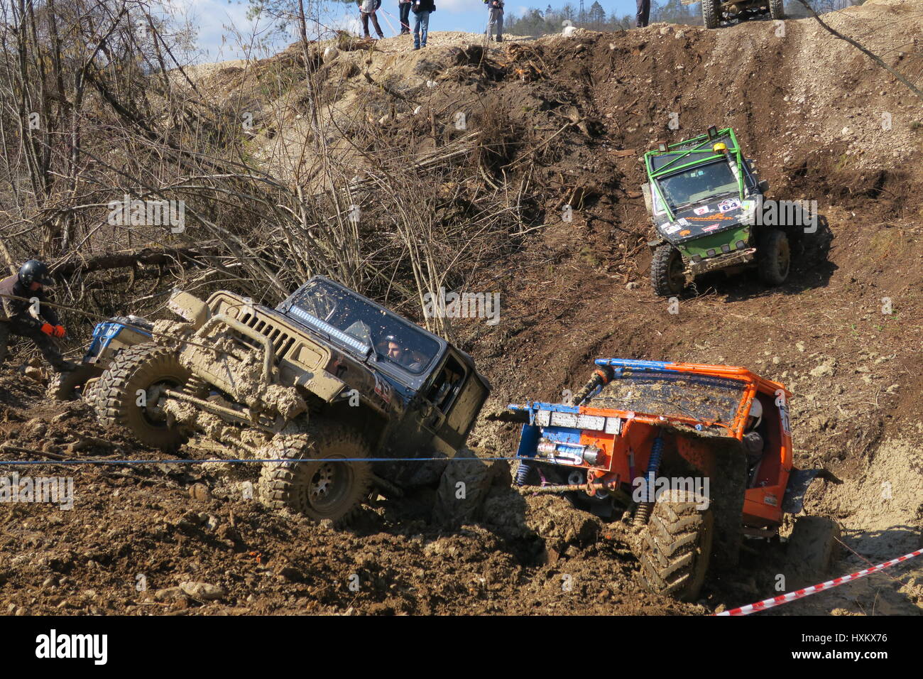 Three off-road cars are pushed uphill, co-driver pulling steel wire at ...