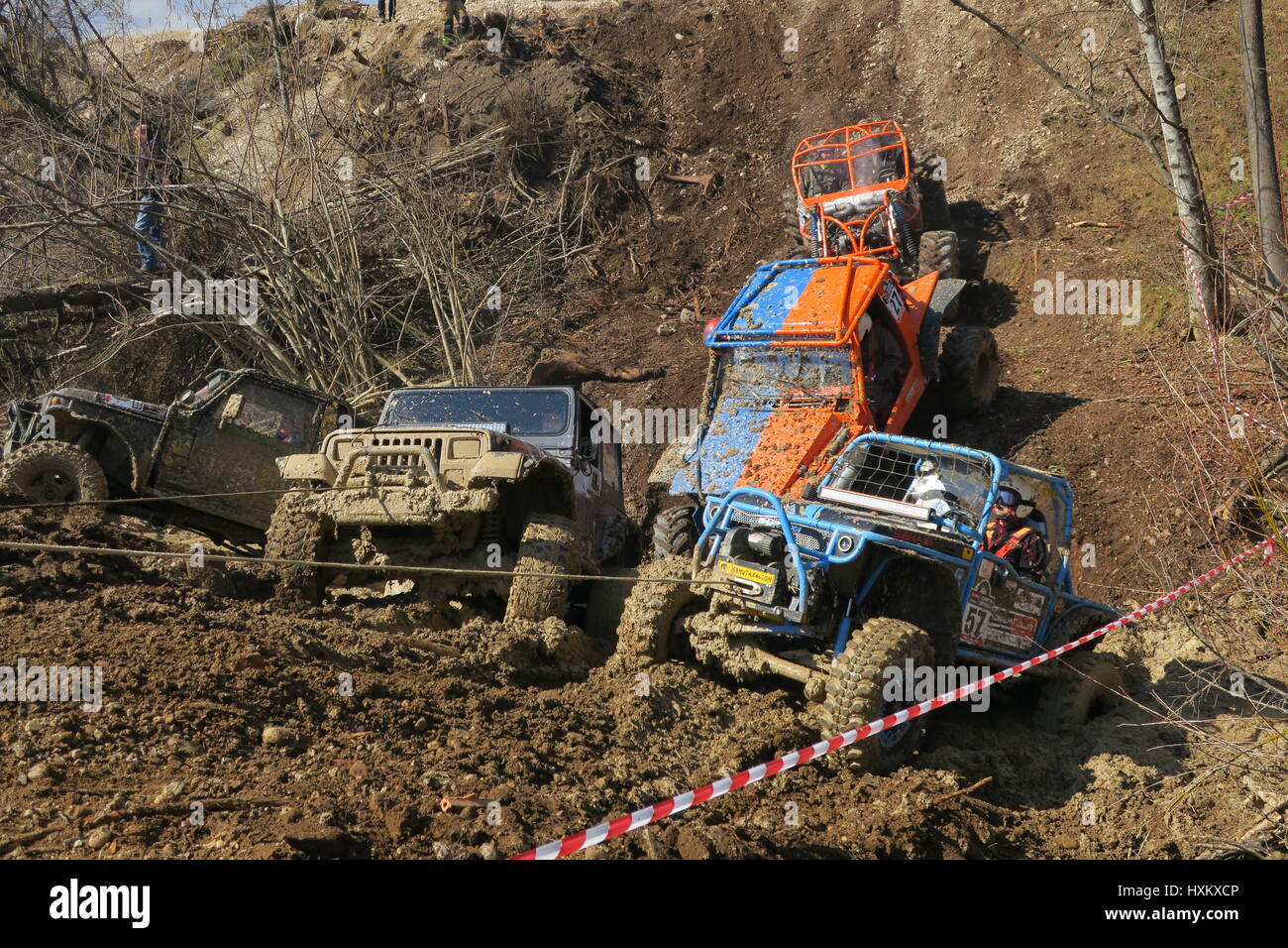 Two off-road cars are pulled uphill by hydraulics of excavator, four ...