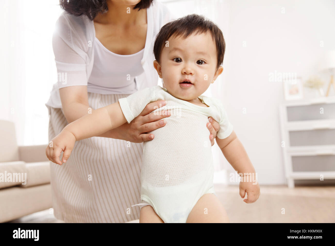 Mother helping baby boy learn to walk Stock Photo - Alamy