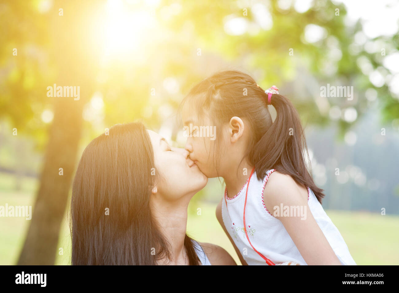 Lifestyle portrait mom and daughter kissing in happiness at the outside in the park. Family ...