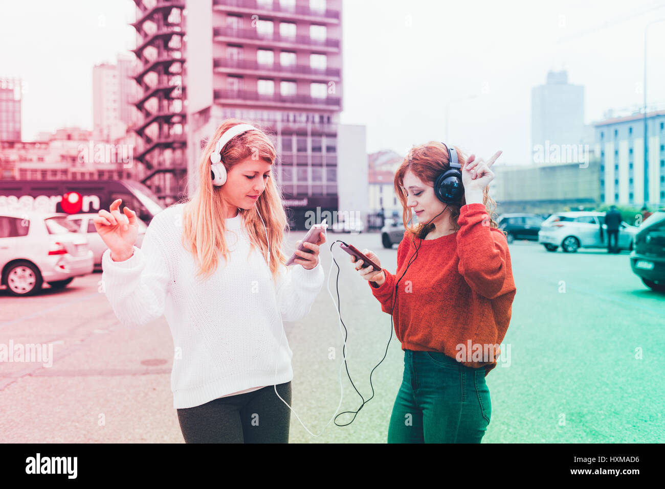 Two young women dancing listening music with smart phone outdoor ...