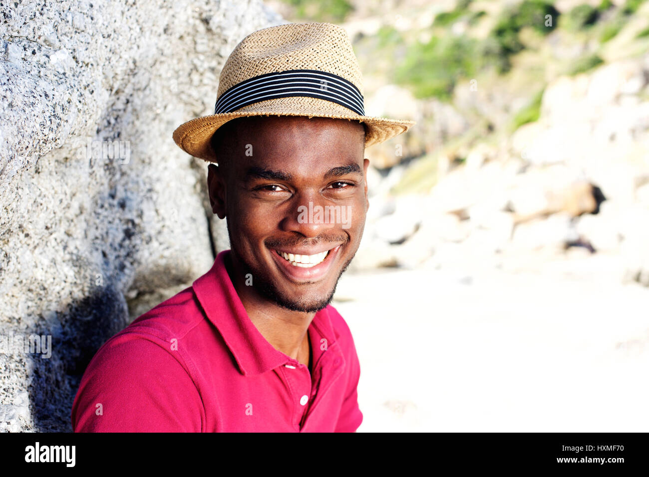 Portrait of handsome young black man with hat smiling at the beach ...
