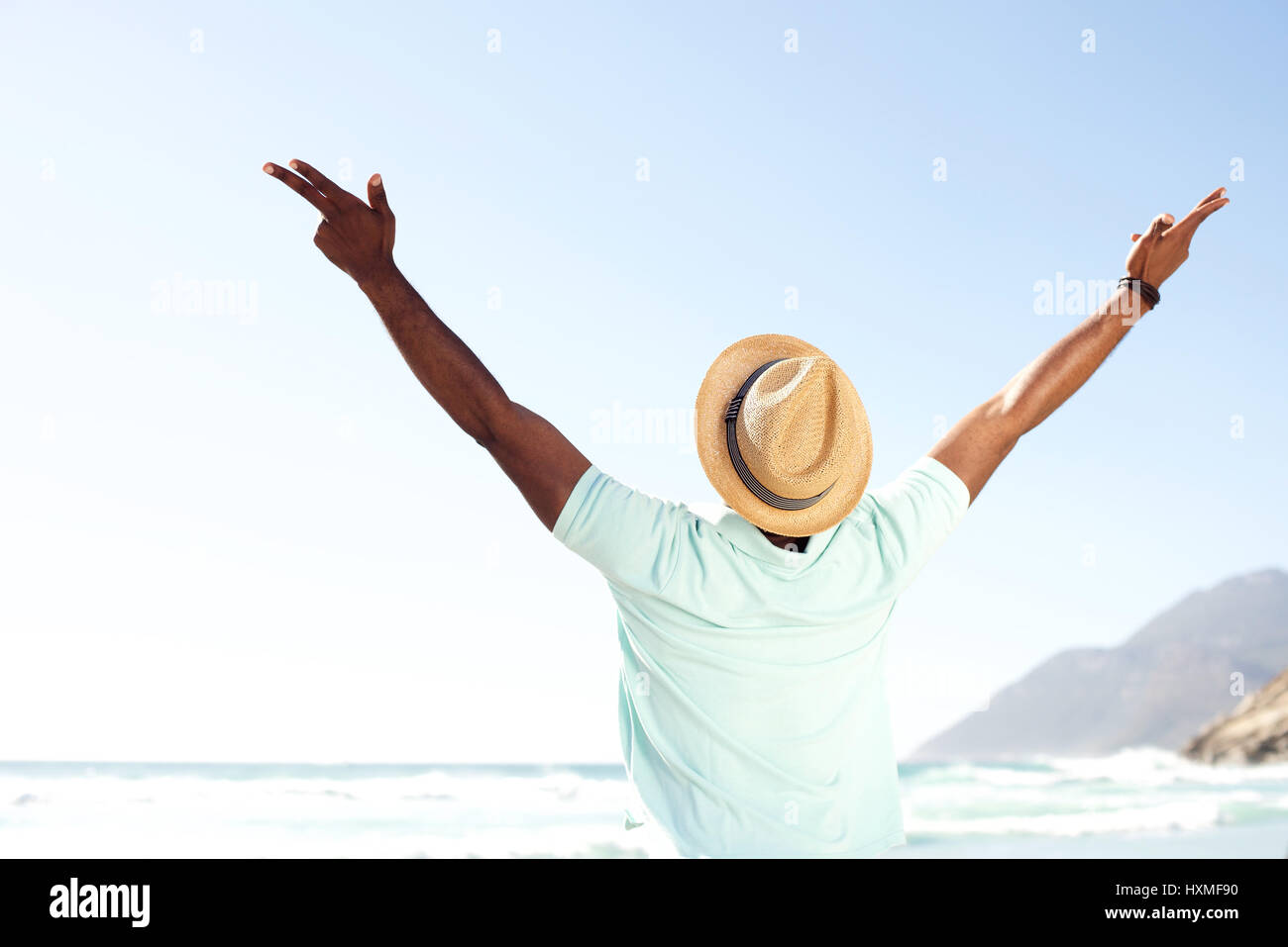 Rear view portrait of young man standing with arms spread open at beach ...
