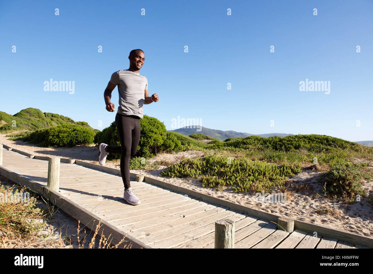 Full body portrait of healthy young african man running on boardwalk at ...