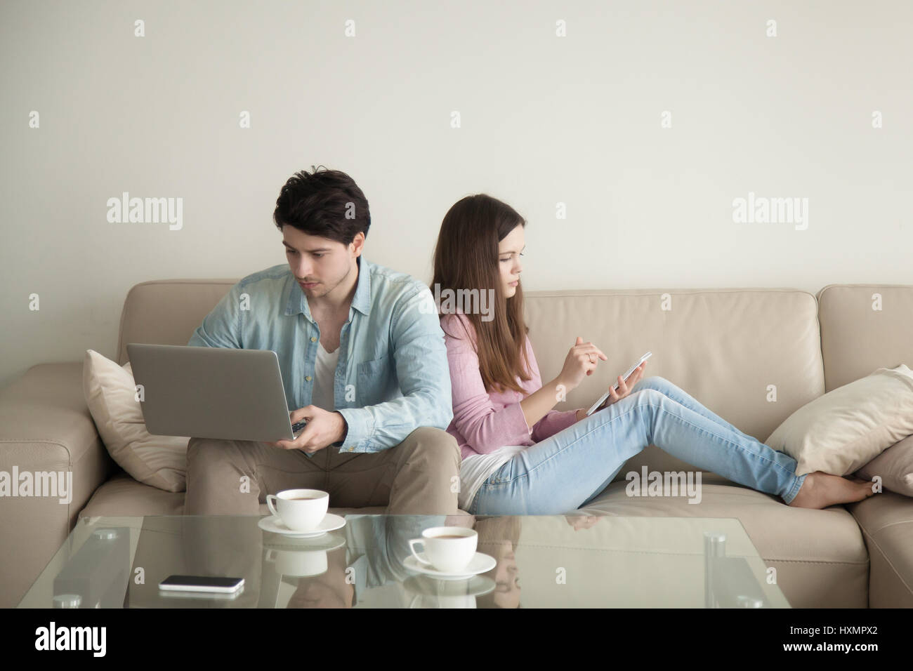 Young man and woman back to back using laptop, tablet Stock Photo - Alamy