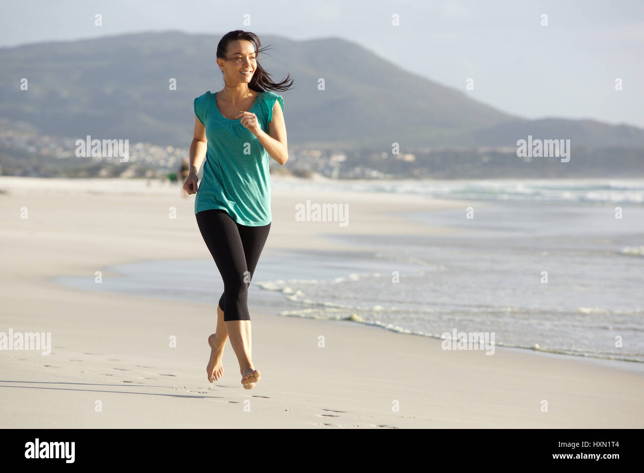 Full length portrait of beautiful young woman running at the beach ...