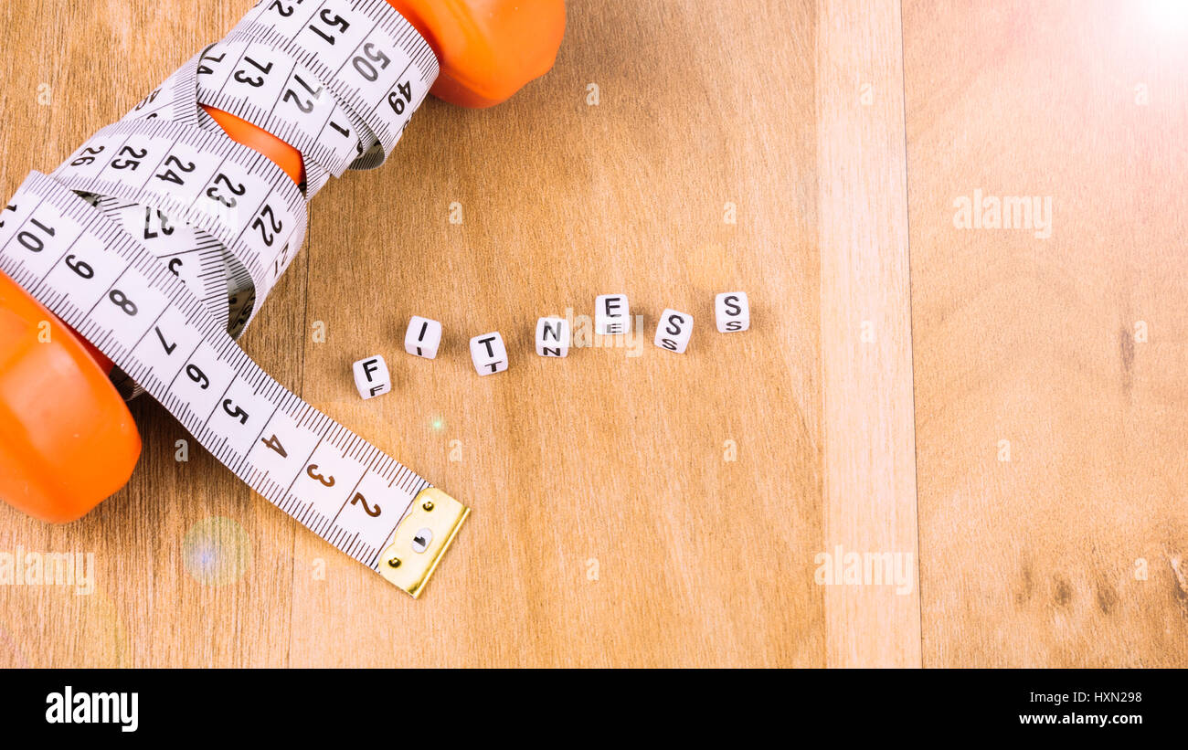 Orange dumbbell with centimetric tape and fitness cube letters on ...