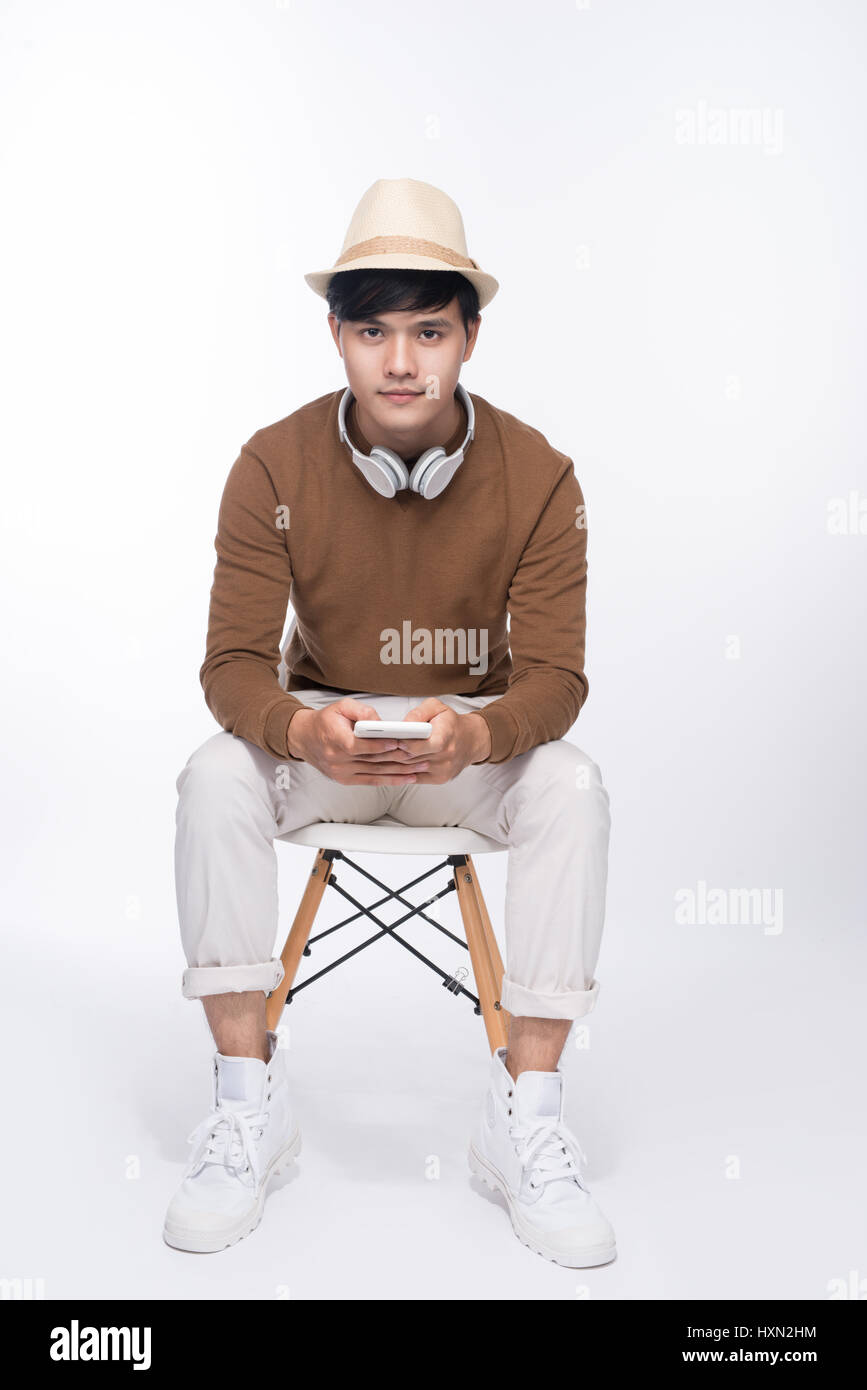 Smart casual asian man seated on chair, holding smartphone in studio ...