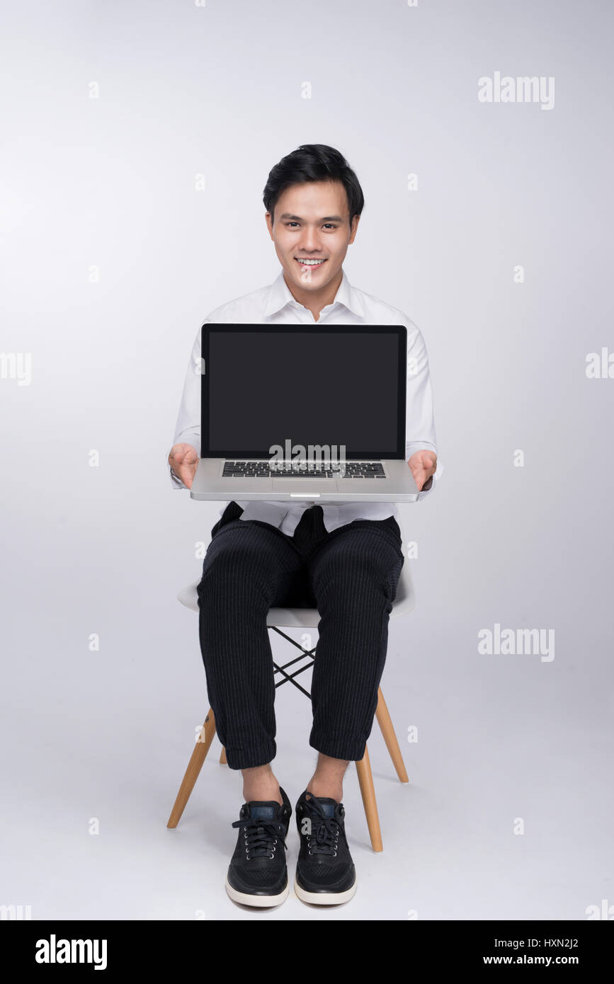 Smart casual asian man seated on chair, showing laptop screen in studio ...