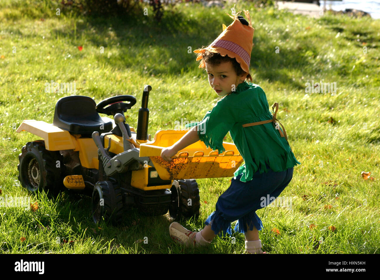 Little child dressed in scarecrow costume with play truck in the yard ...