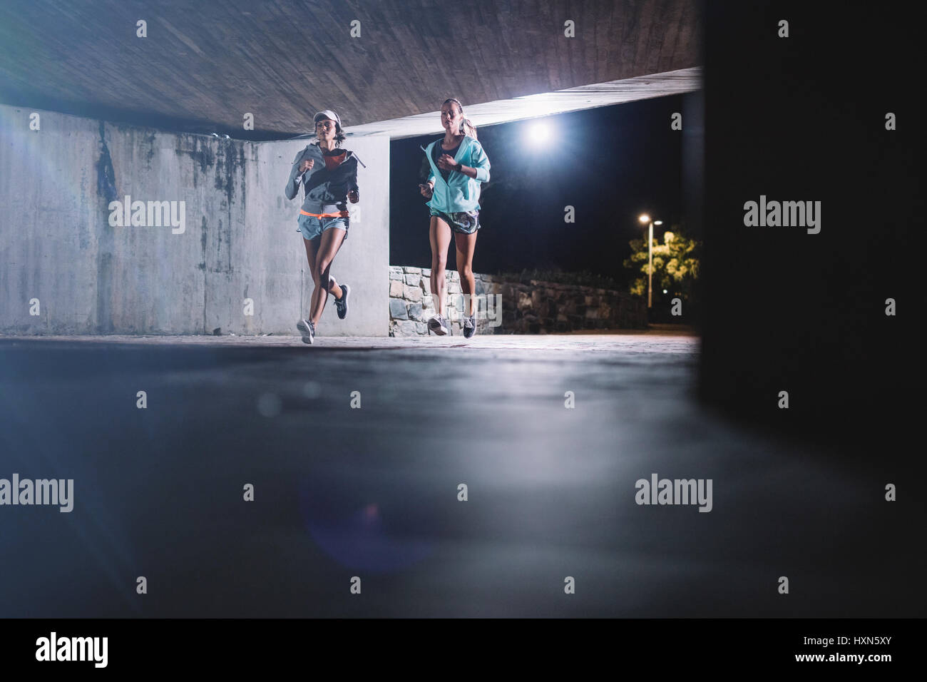 Two young female runners running together at night in city. Young women ...