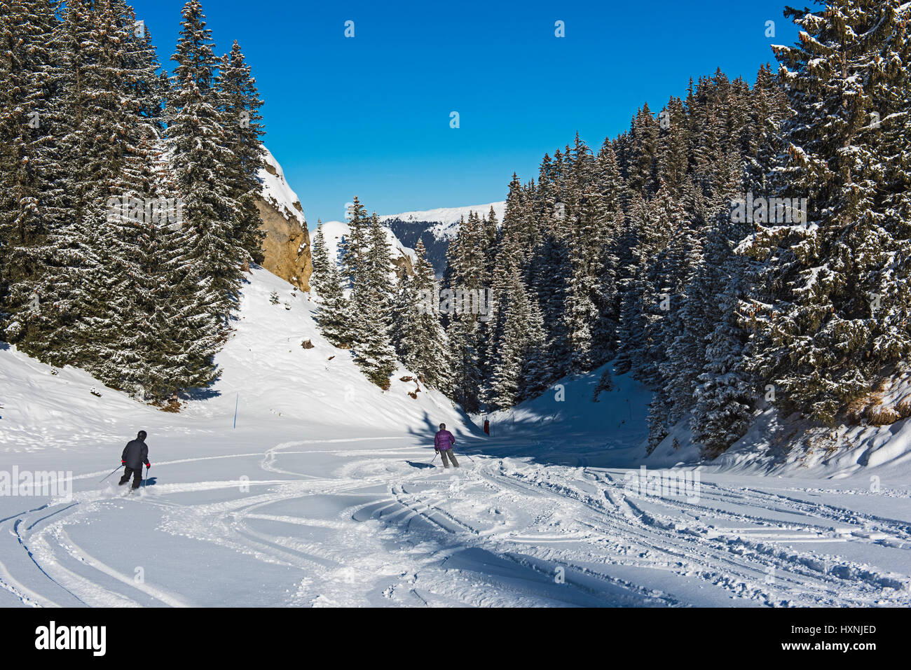 Skiers on a ski slope piste in winter alpine mountain resort with ...