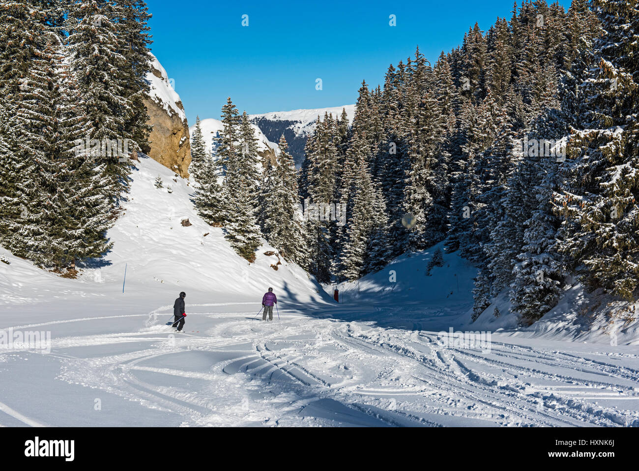 Skiers on a ski slope piste in winter alpine mountain resort with ...