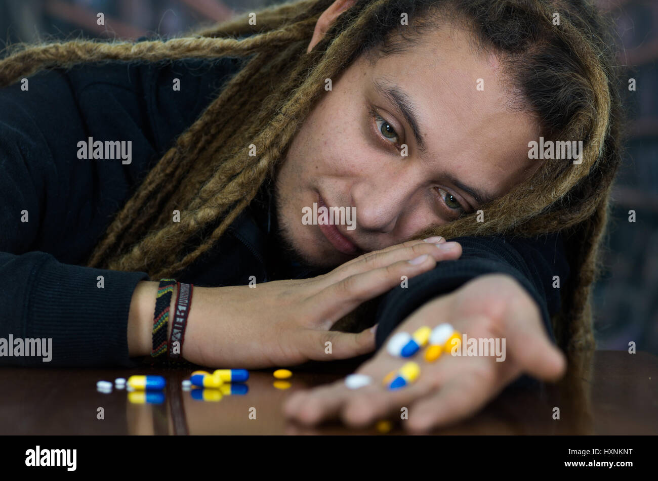 Man lying over table with dopey facial expression, colorful pills lying ...