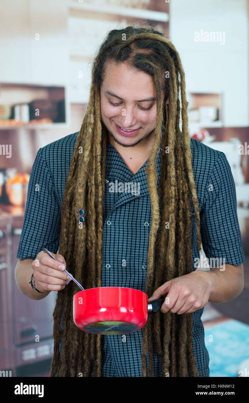 Man with dreads and hippie look posing for camera holding red cooking ...