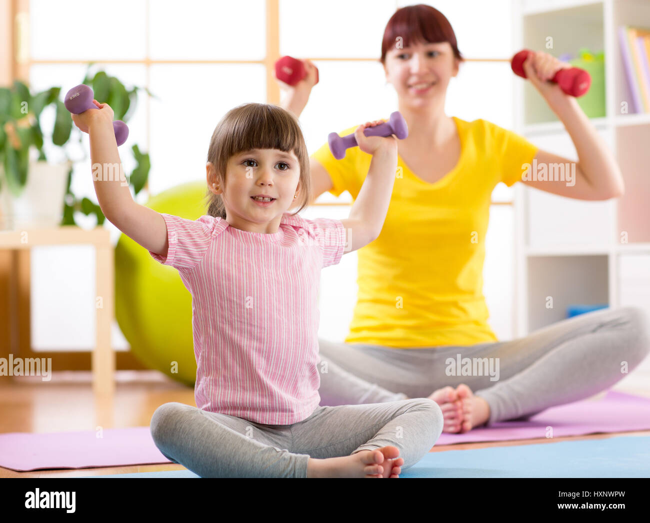 Woman and her child daughter doing fitness exercises with dumbbells ...