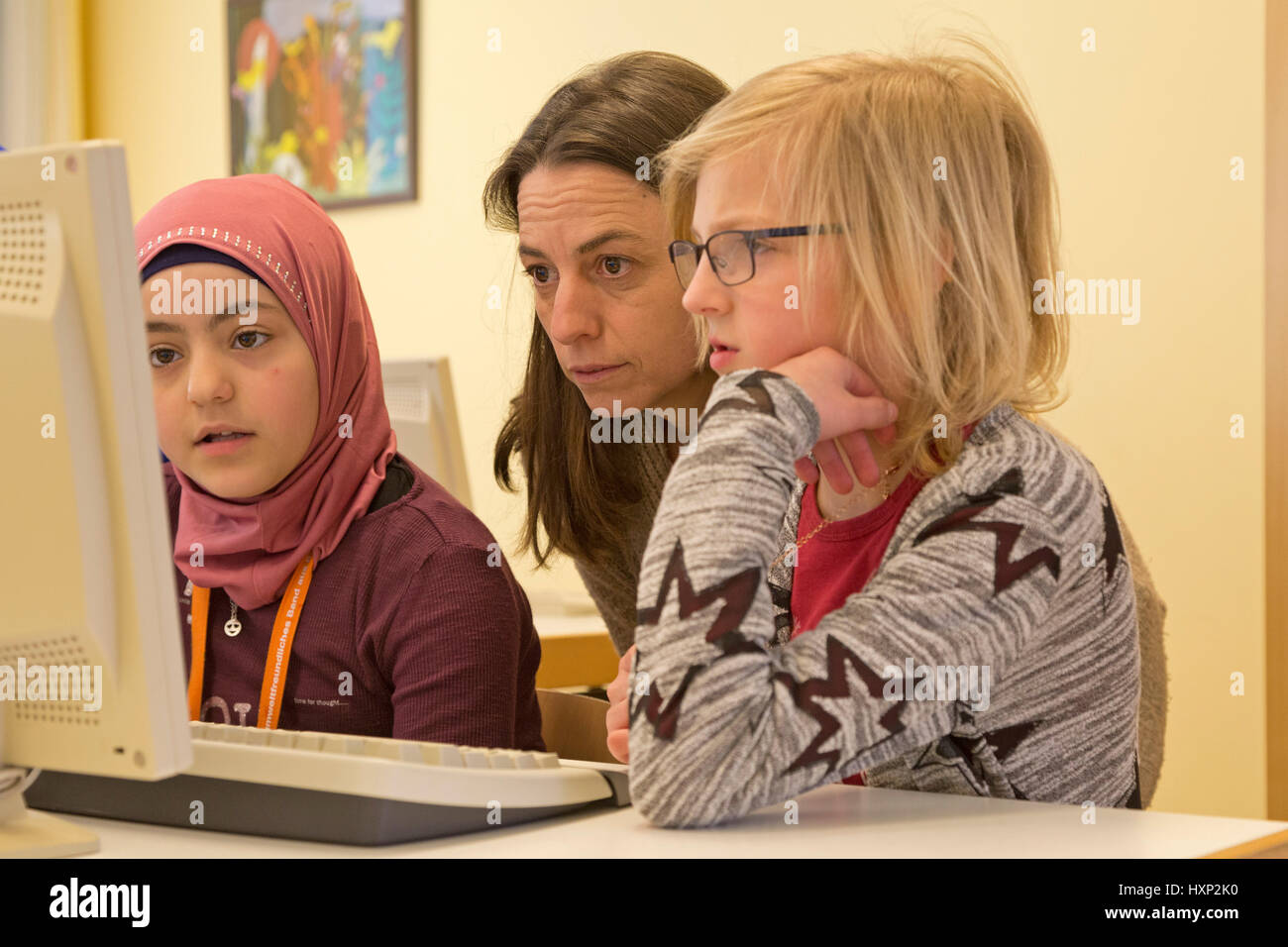 girls at primary school working with a computer, their teacher helping ...