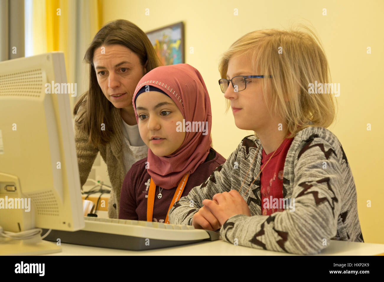 girls at primary school working with a computer, their teacher helping ...