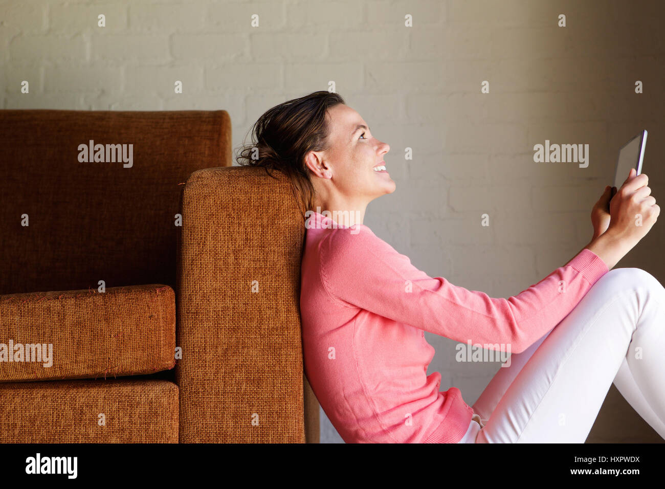 Side portrait of young woman sitting by a sofa at home with digital ...