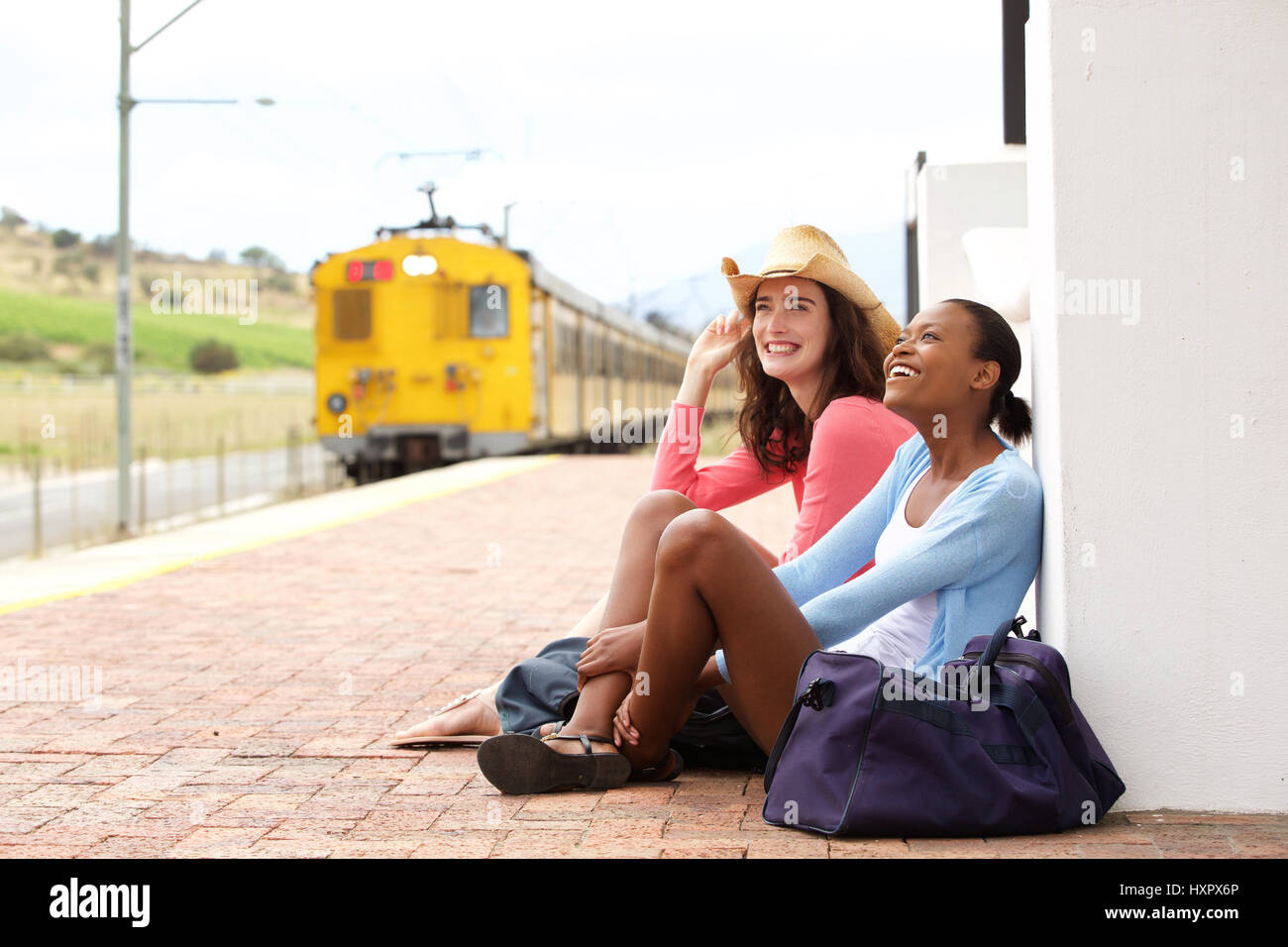 Portrait of two young female friends sitting at railroad station and ...