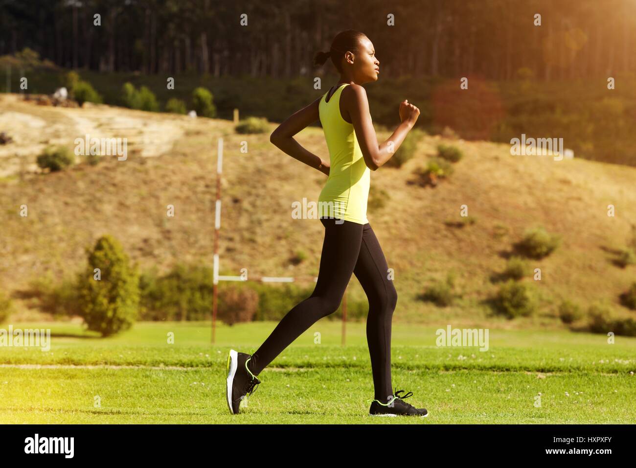 Side view full body portrait of a young african woman jogging outdoors ...