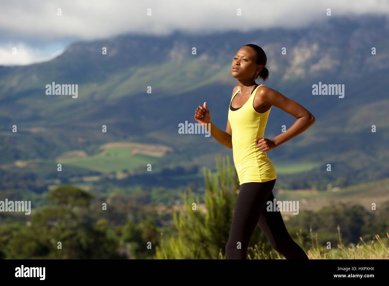 Side portrait of fit young african woman running outdoors in nature ...