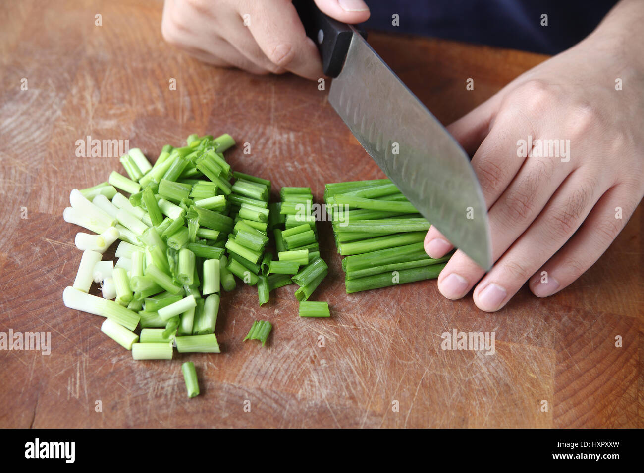 A man uses a chef’s knife to chop up scallions on a cutting board Stock ...