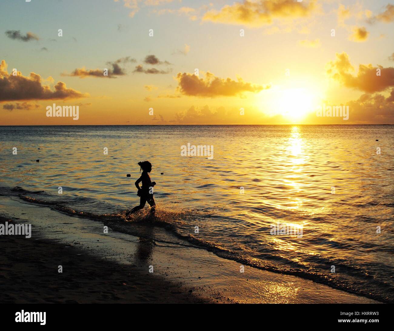 A girl plays in the golden ripples created by a beautiful sunset in ...