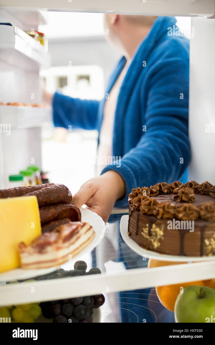Fat guy take plate full of hard high calories food from refrigerator ...