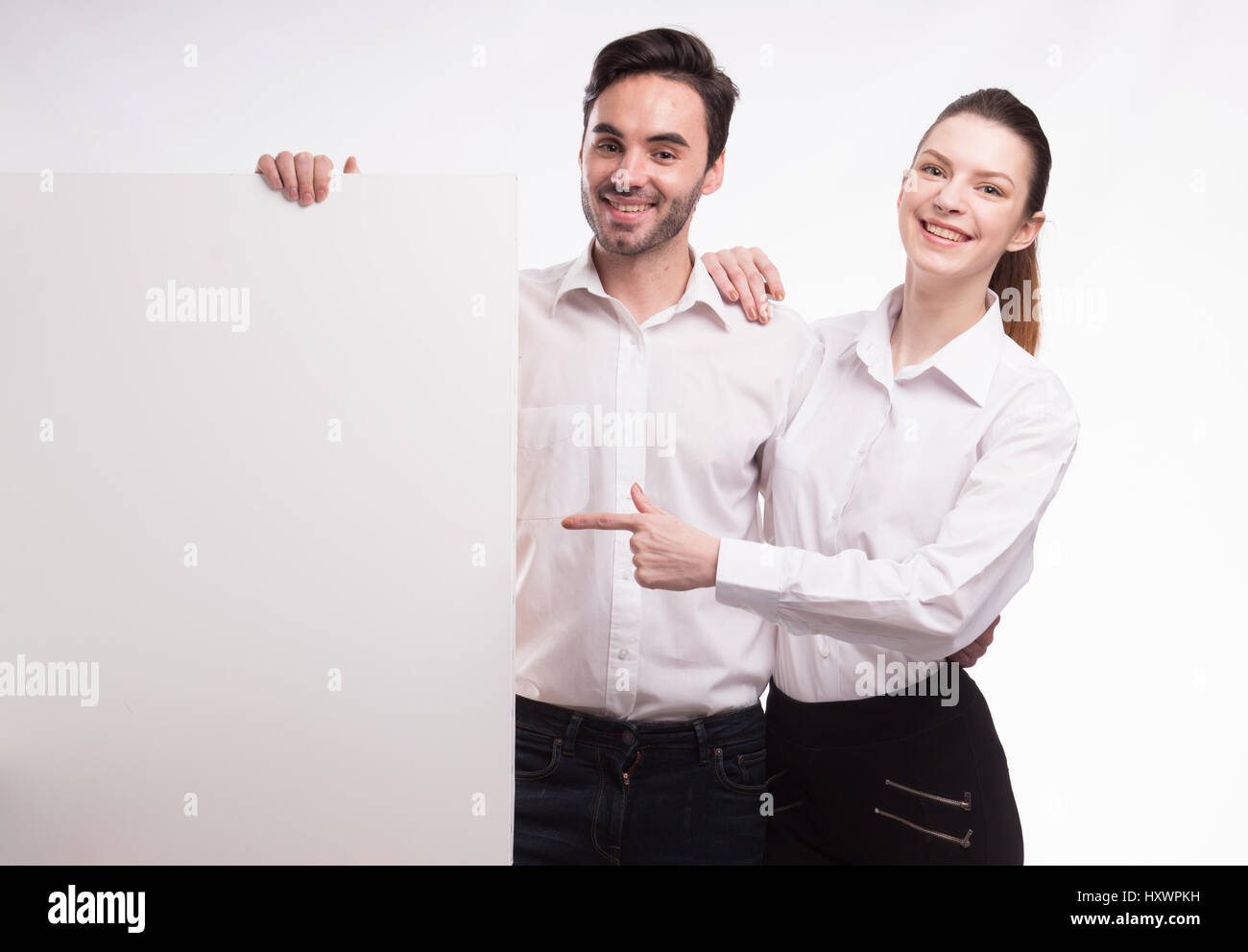 Young happy couple showing presentation pointing on placard over gray ...