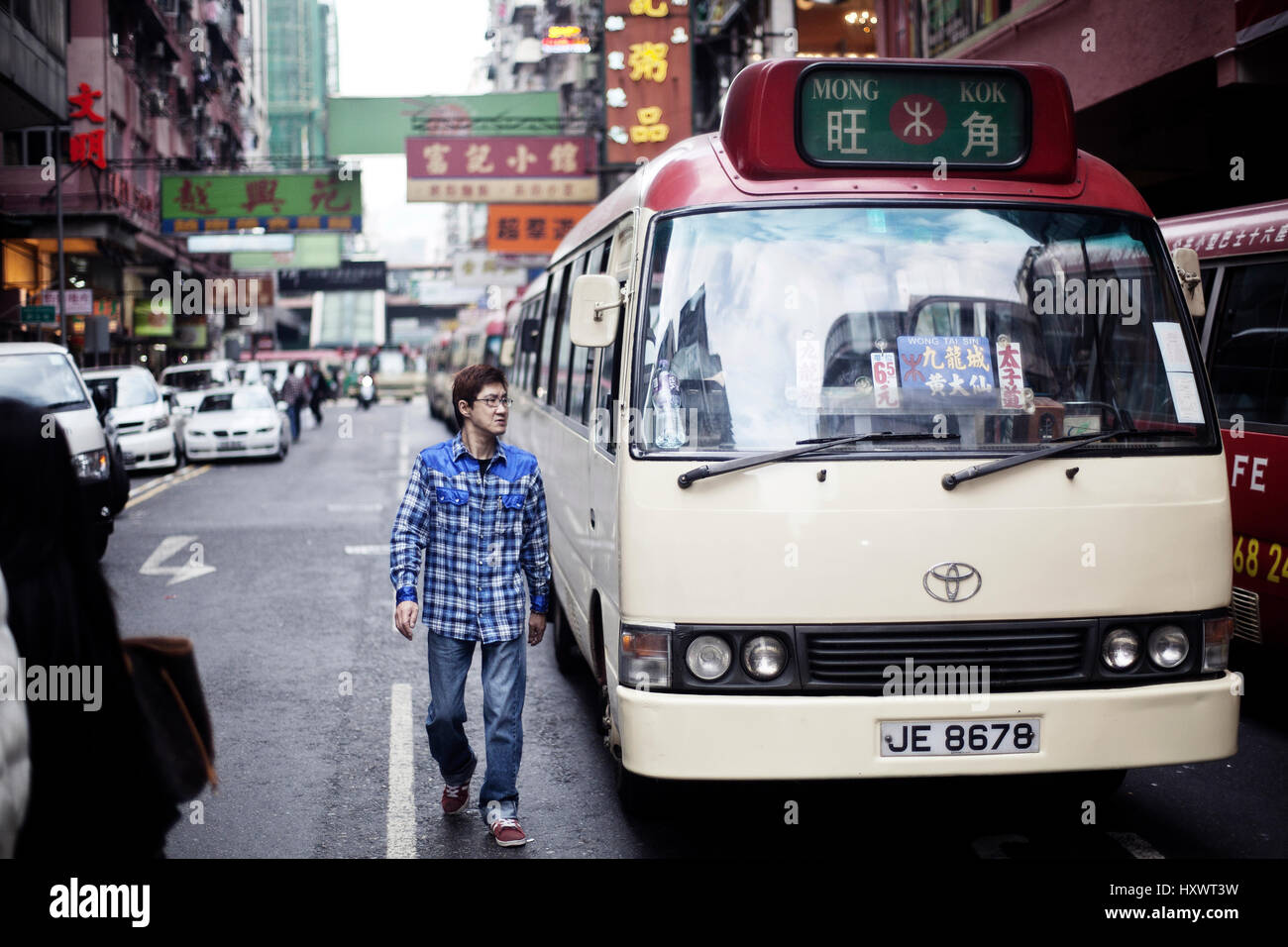 A Chinese man is walking next to a bus in Hong Kong, China. There are ...