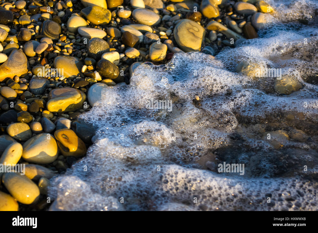 sea pebble beach with multicoloured stones, transparent waves with foam ...