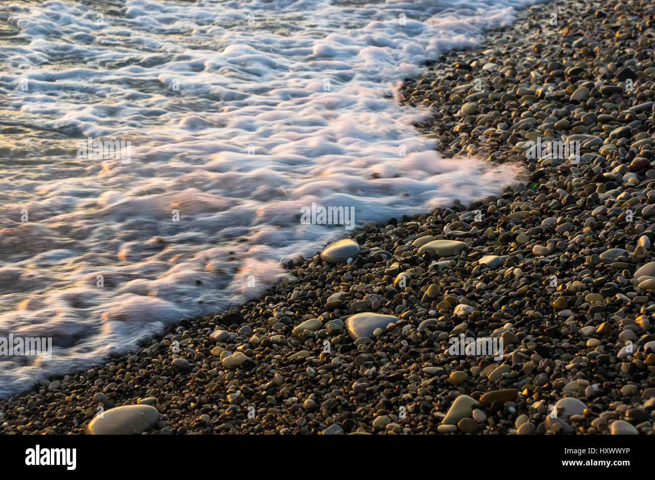 sea pebble beach with multicoloured stones, transparent waves with foam ...